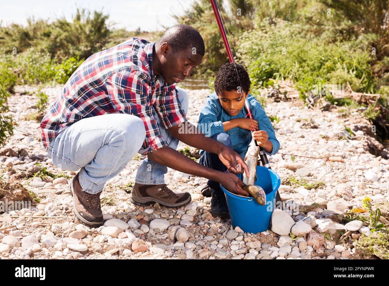 Portrait of afro fisherman and his little son holding fishing rod with ...