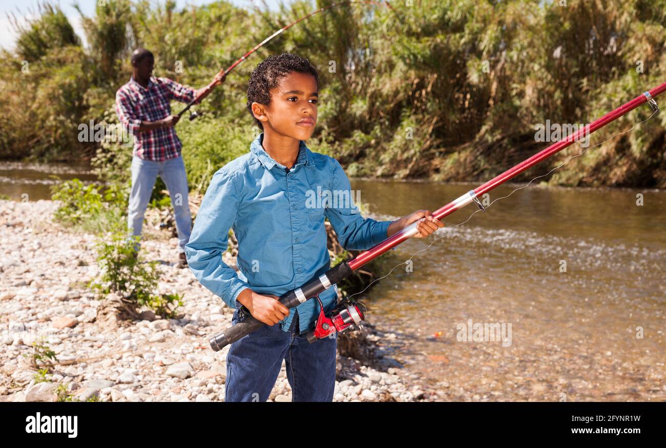 Afro boy holding fishing rod and pulling fish from river Stock Photo ...