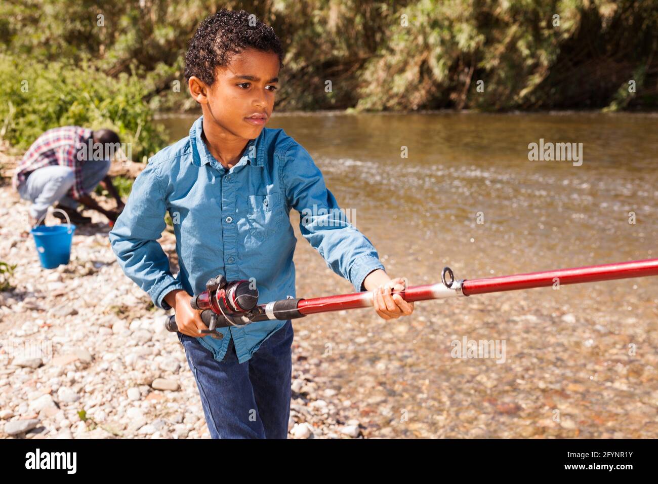 Afro boy holding fishing rod and pulling fish from river Stock Photo ...