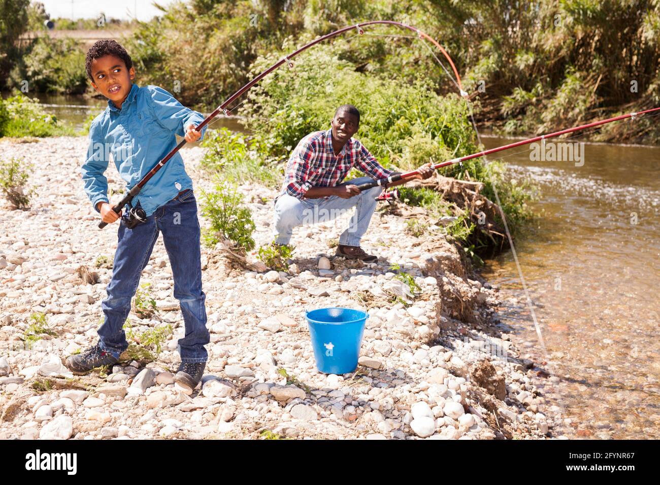 Afro boy holding fishing rod and pulling fish from river Stock Photo ...