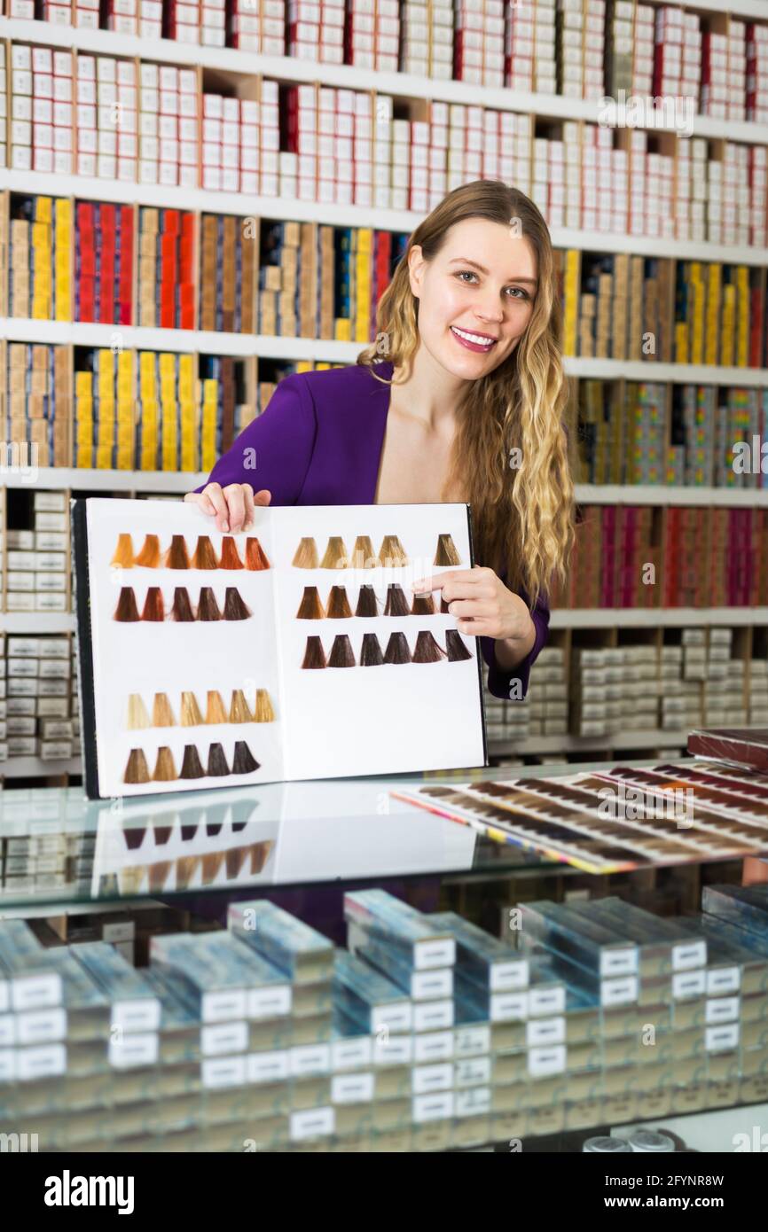 Smiling female seller offering stylish colors of hair dye on palette in ...
