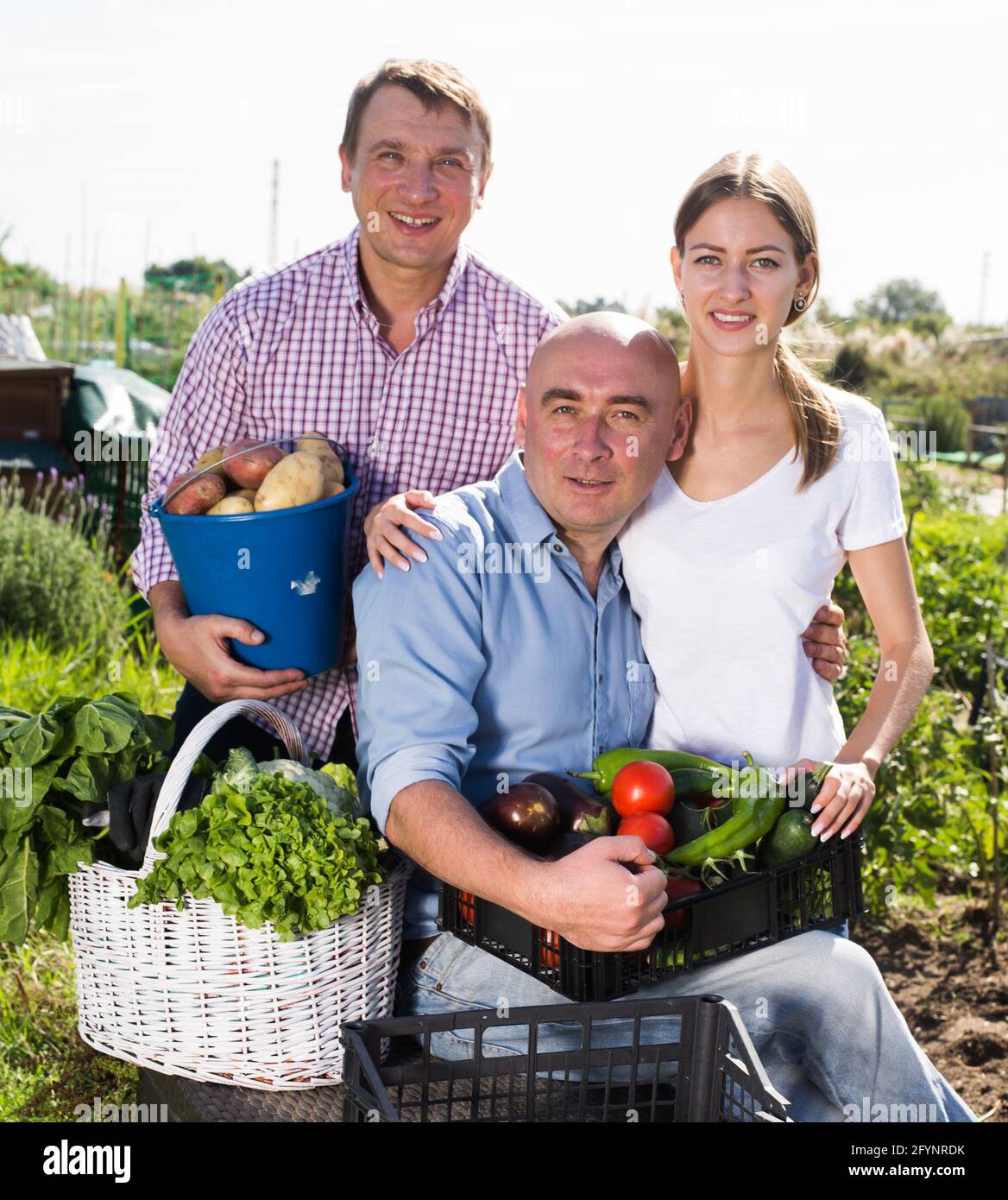 Happy family of three gardeners posing with harvest of vegetables and ...