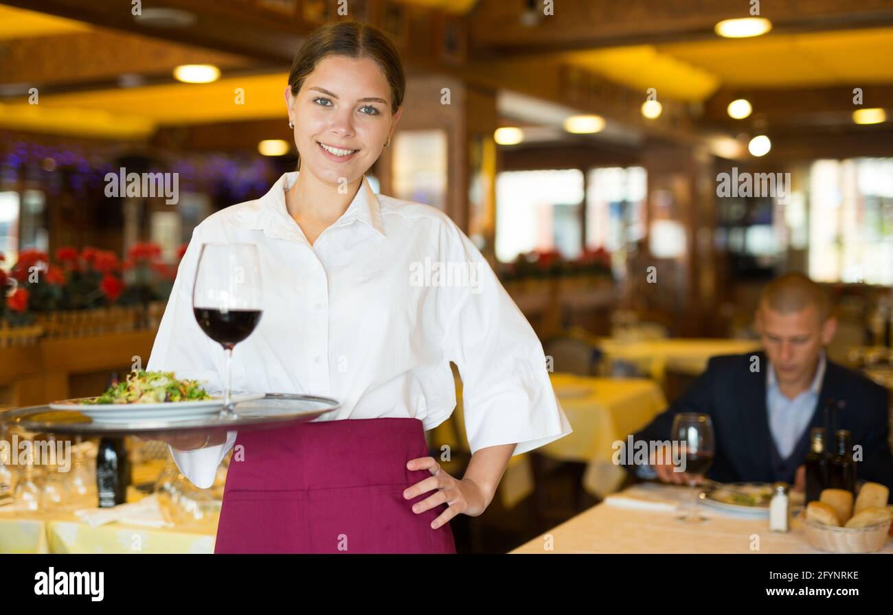 Polite waiter holding tray at restaurant with customers behind him ...