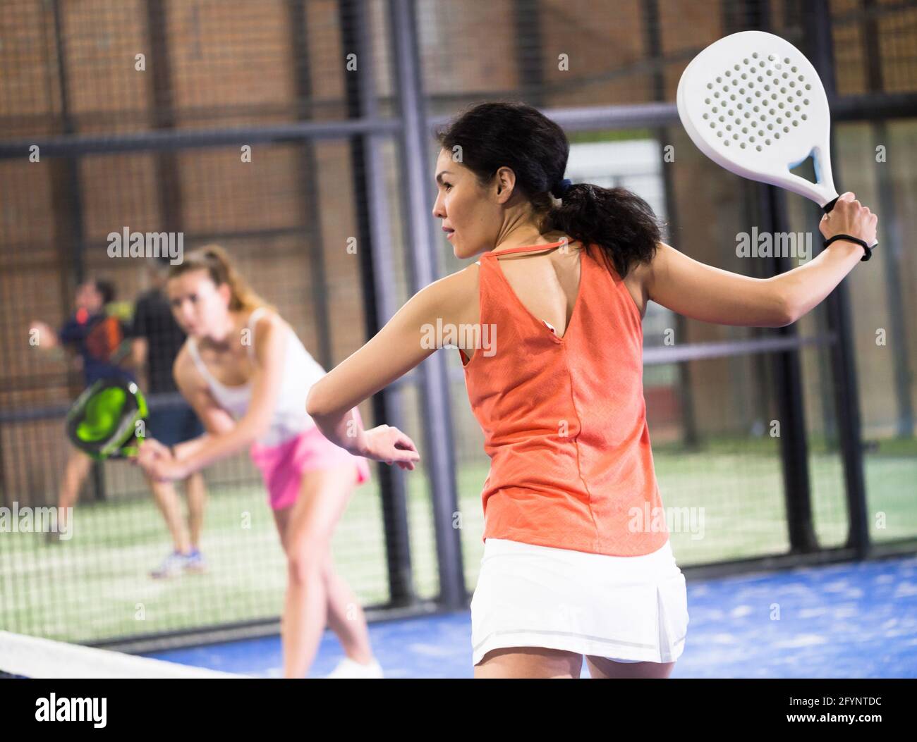 Woman playing padel in a green grass padel court indoor behind the net ...