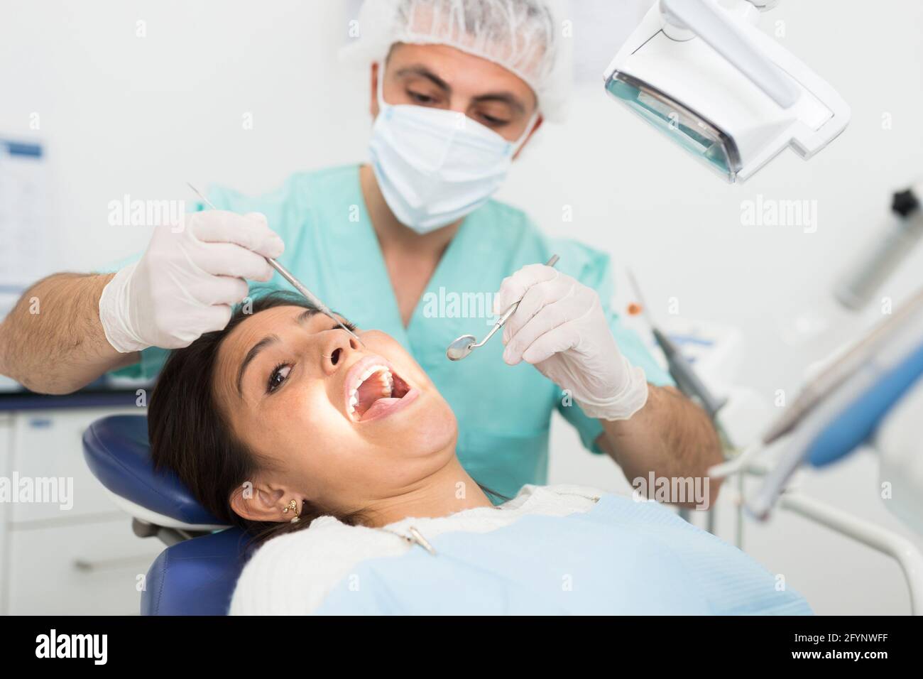 Dentist man examining a latin female patient teeth with dental tools - mirror and probe Stock ...