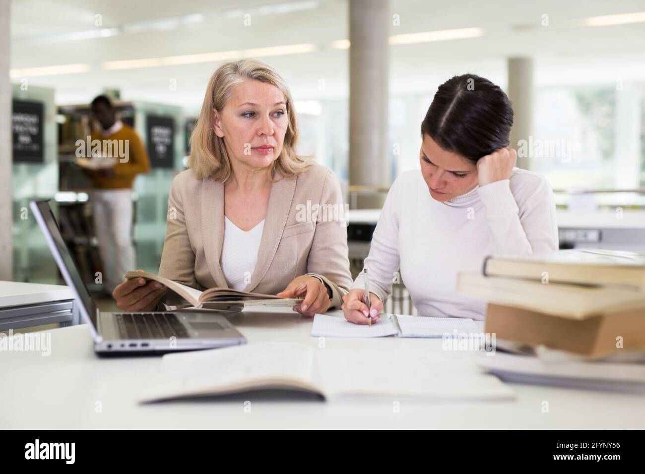 Friendly female tutor helping to diligent positive girl preparing for ...