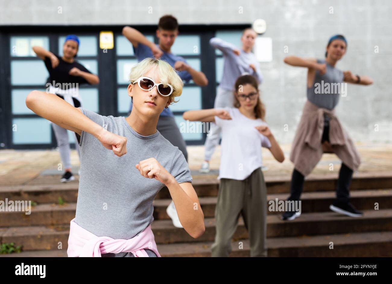 Positive teen boy dancing modern street dance outdoors with teenagers ...