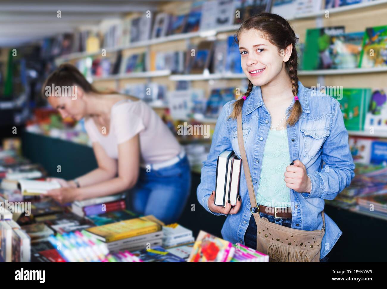 Portrait of positive teenage girl picking book in book shop Stock Photo ...