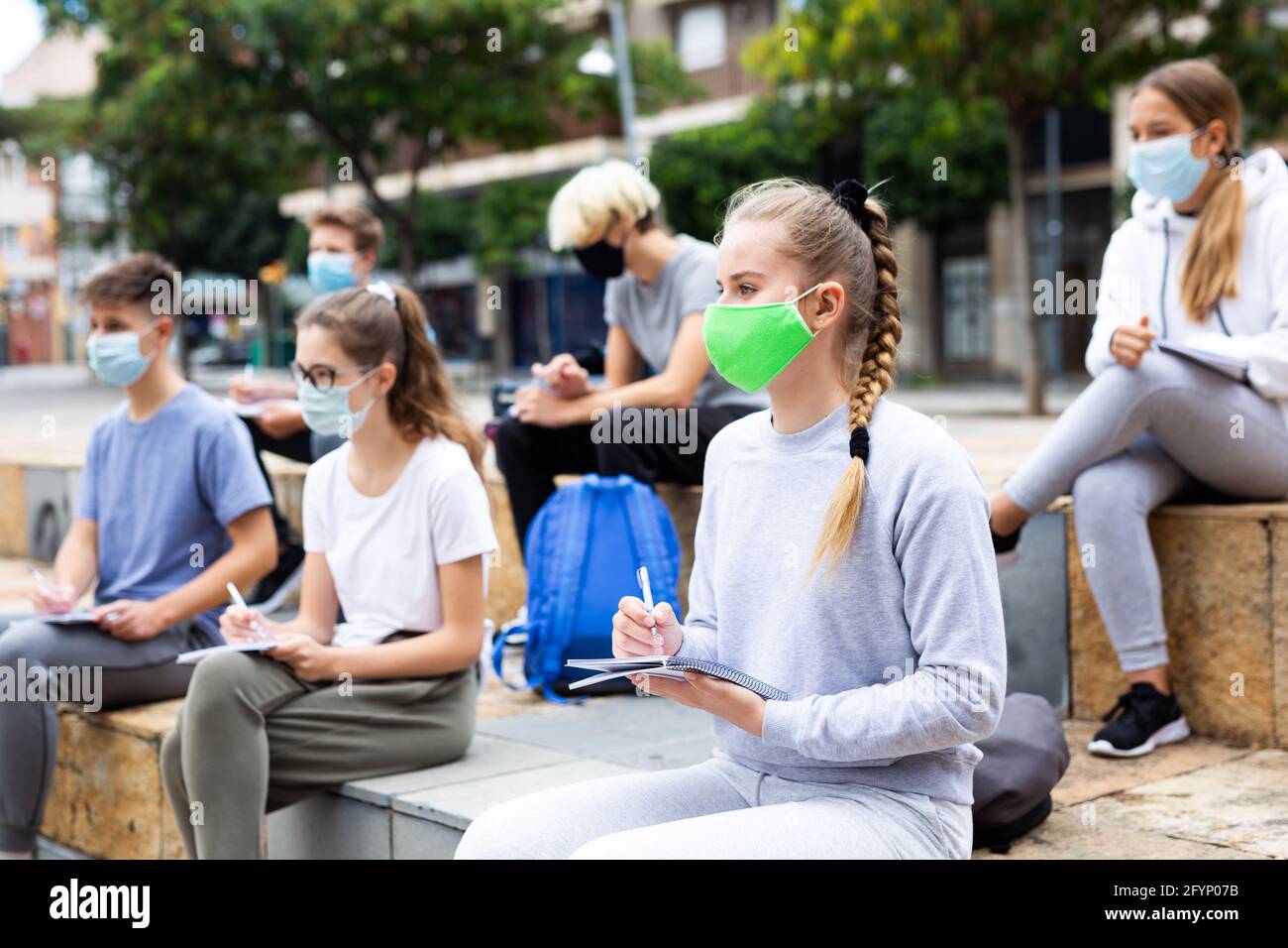 Students in protective masks record lecture while sitting on a stone ...