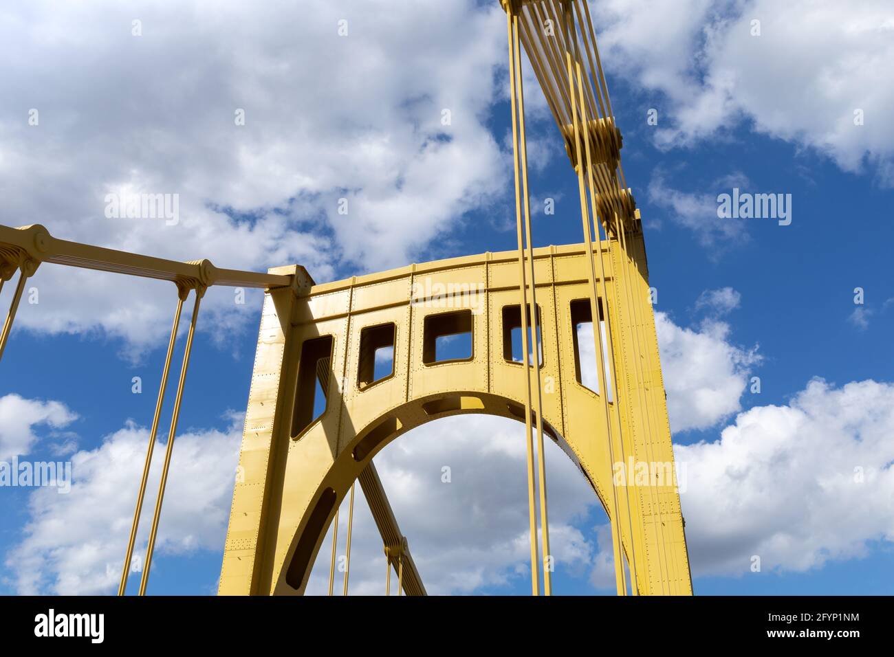 Bright yellow metal bridge structure against a blue sky with clouds ...