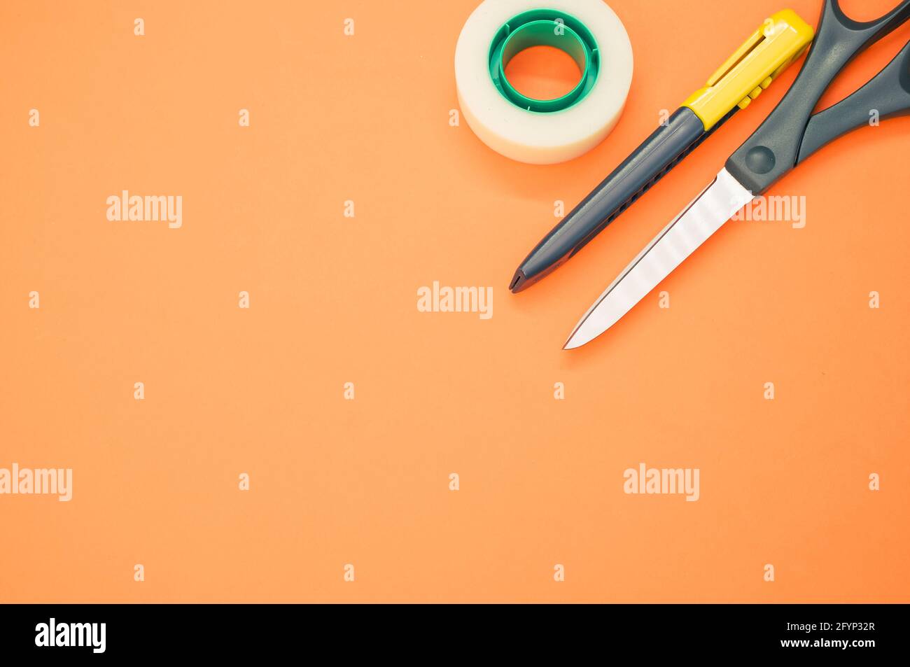 Closeup shot of scissors adhesive tape and a utility knife on an orange ...