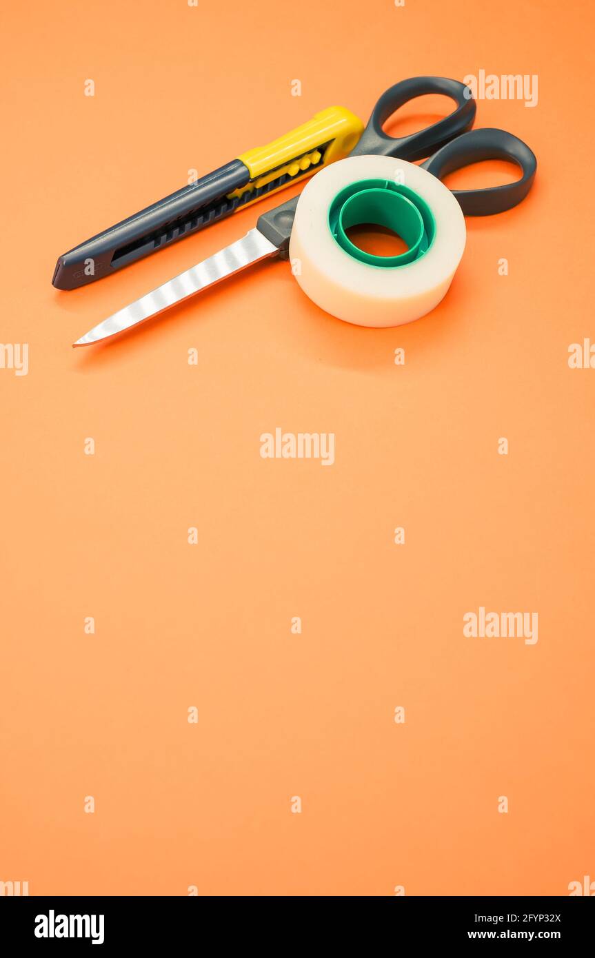 Closeup shot of scissors adhesive tape and a utility knife on an orange ...