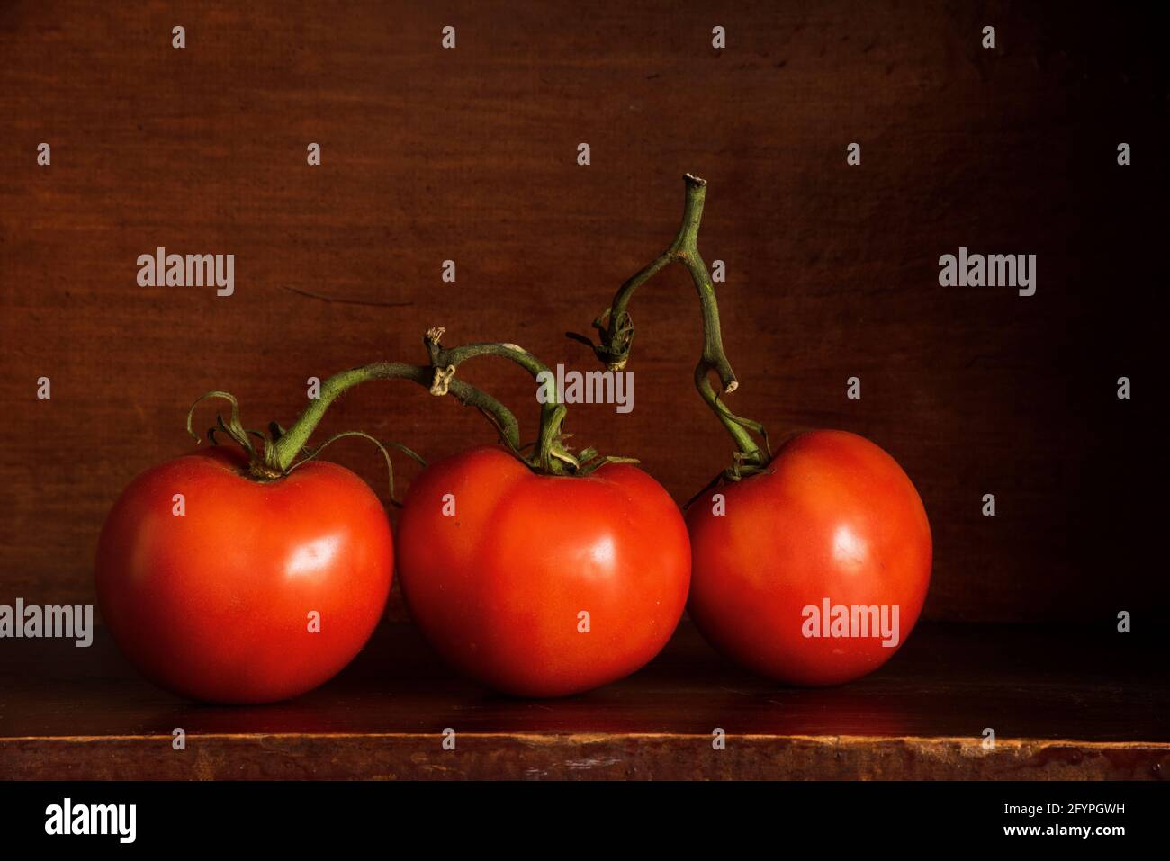 A trio of tomatoes are displayed on a wooden shelf in a still life ...
