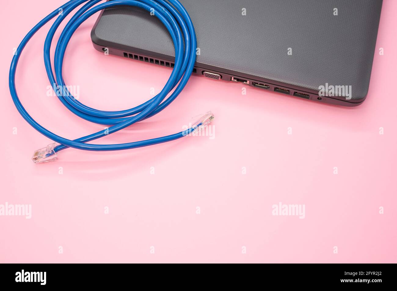 A high angle shot of a LAN cable on a laptop against a pink background ...