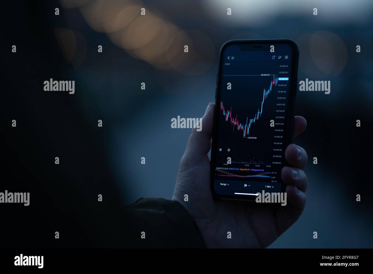 Trader holding smartphone with financial chart and analyzing price flow ...