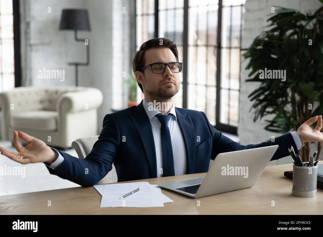 Peaceful business leader meditating at workplace, making zen hands ...