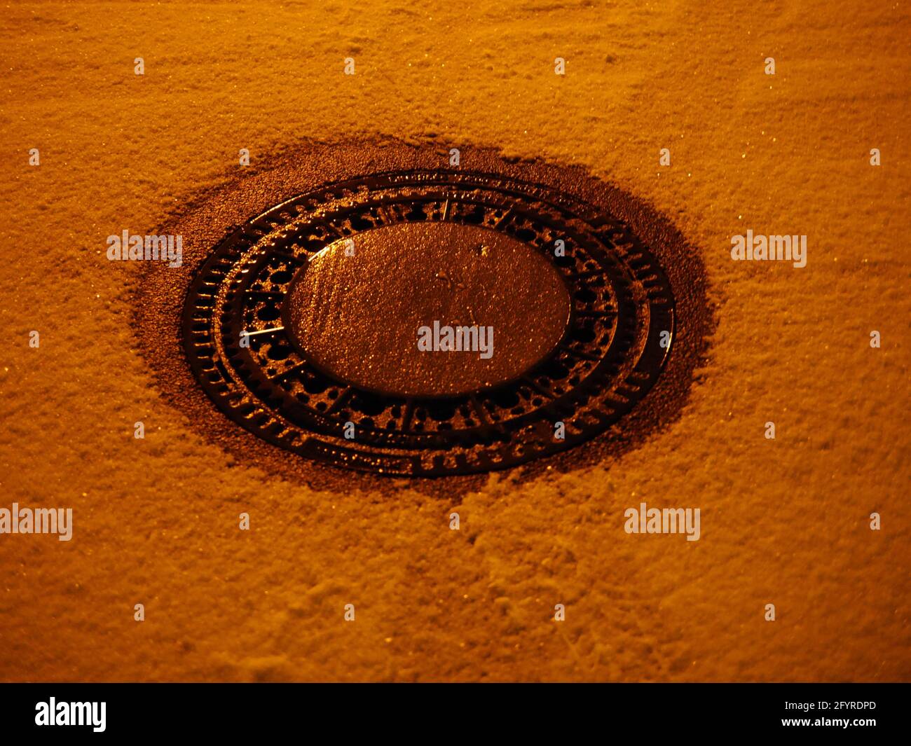 Manhole cover in street lighting on a snow-covered road Stock Photo - Alamy