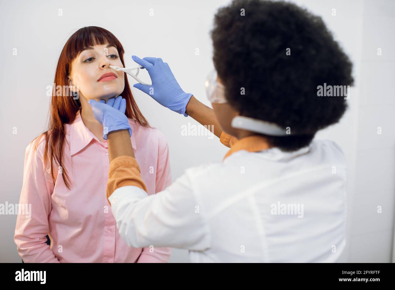 Back view of female afro doctor ent, doing nose examination of her ...