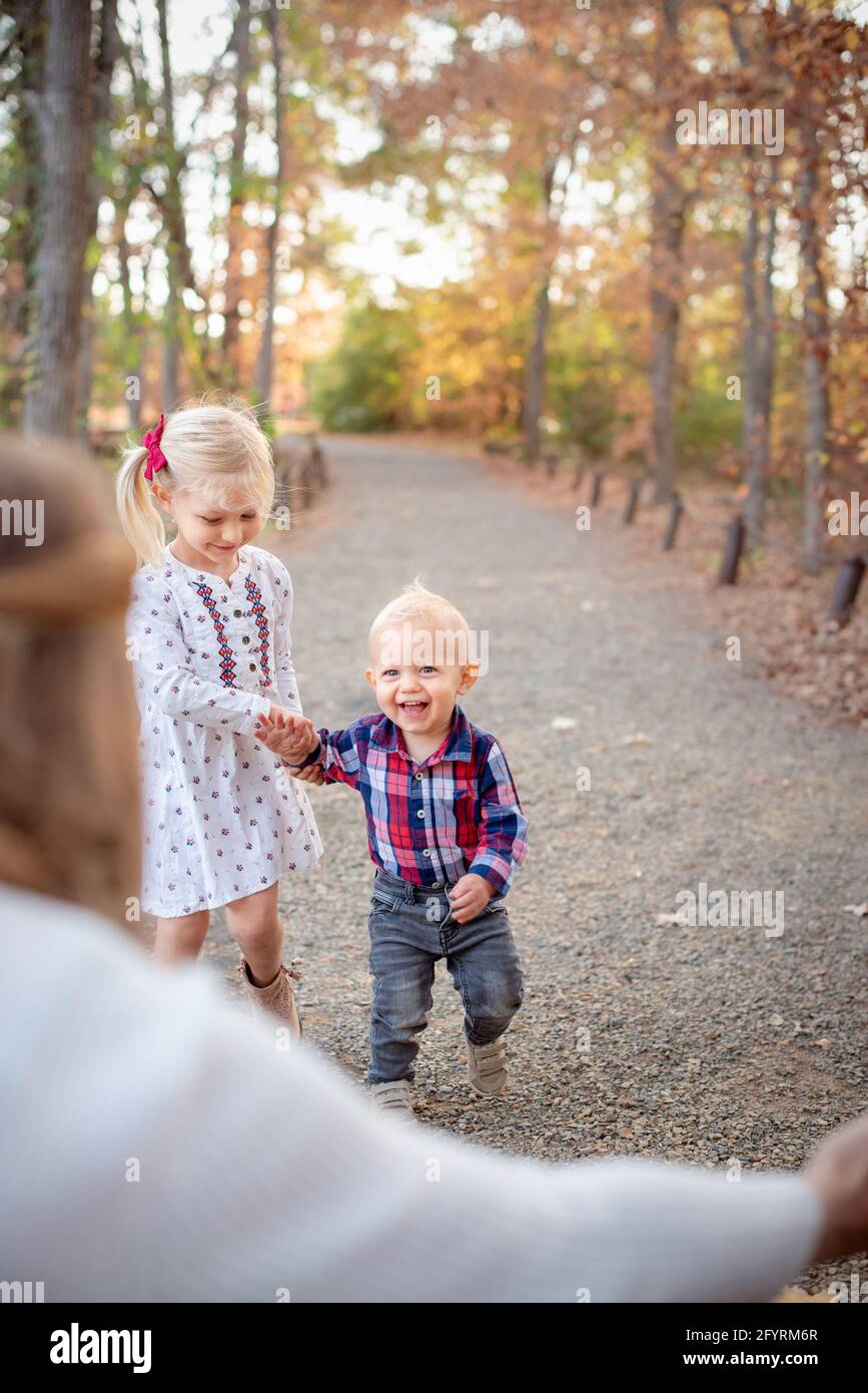 Shallow focus shot of little blonde kids holding hands and running to ...