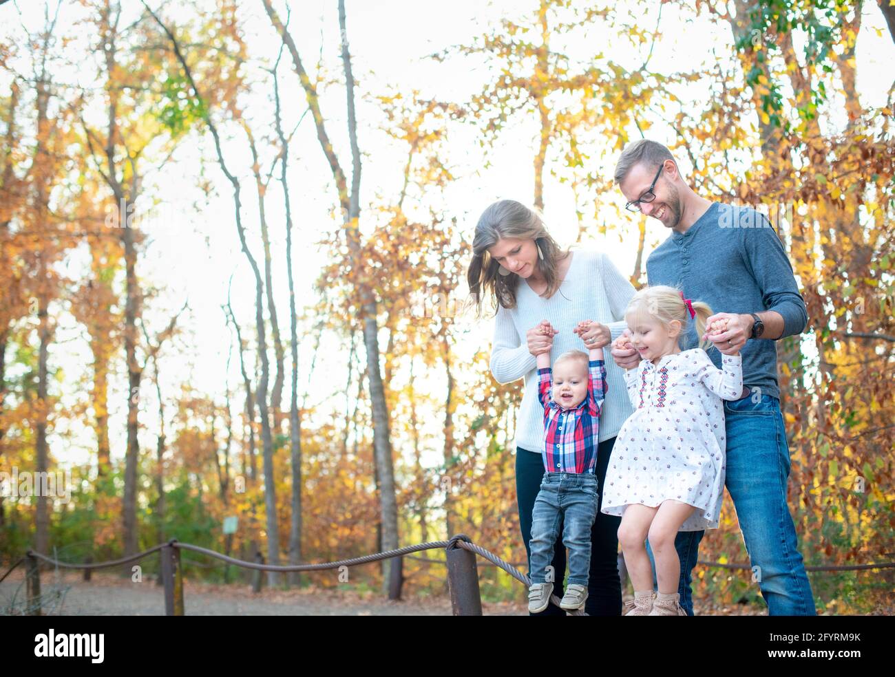 Adorable family of four holding hands on a road that goes through a forest in Texas Stock Photo ...
