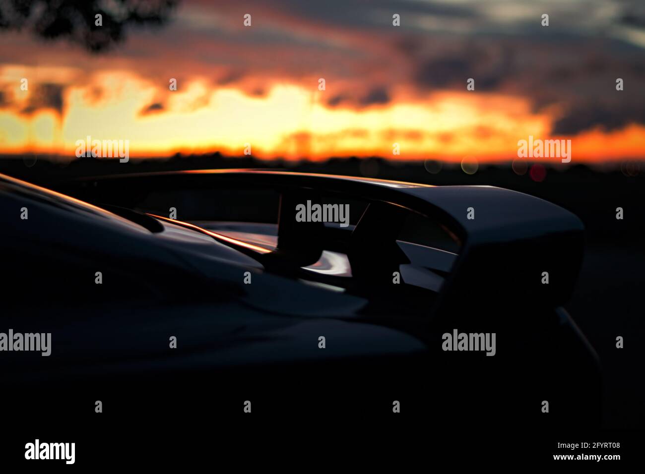 A closeup shot of a black sports car back with a wing against a sunset ...