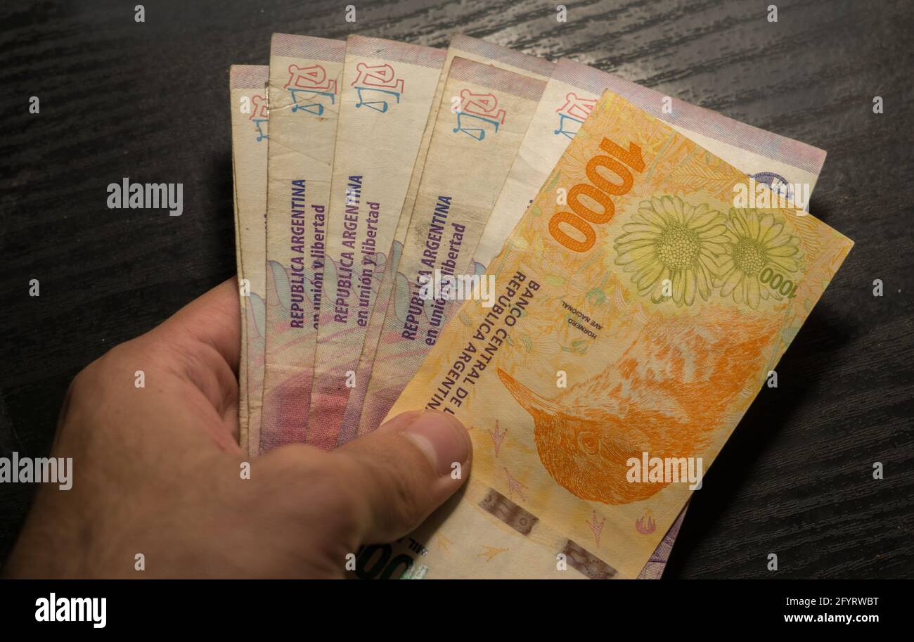 A charitable man's hand giving away a pile of 1000 Argentine pesos ...
