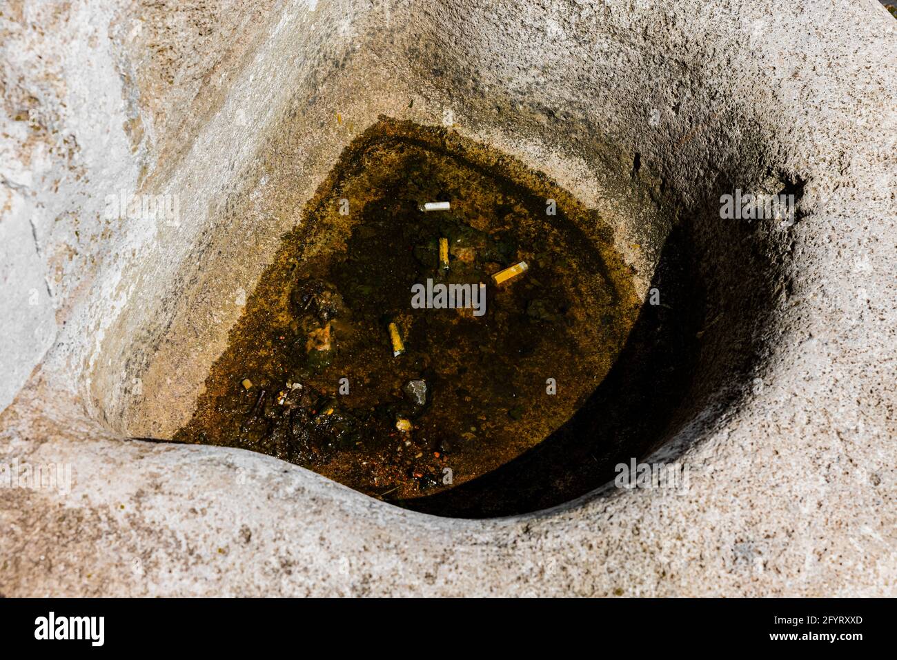 A closeup of dirty water in the dried stone fountain with cigarette ...