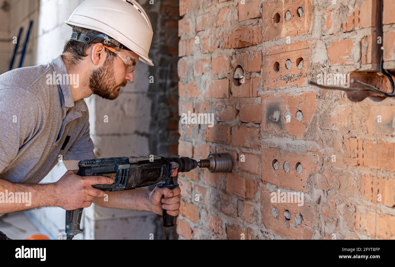 Handyman at a construction site in the process of drilling a wall with ...