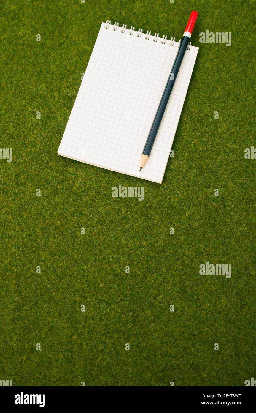A top view shot of a spiral notebook and a pen on a green grass surface ...