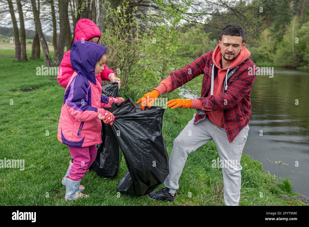 Two little girls with their dad, with garbage bags on a trip to nature ...