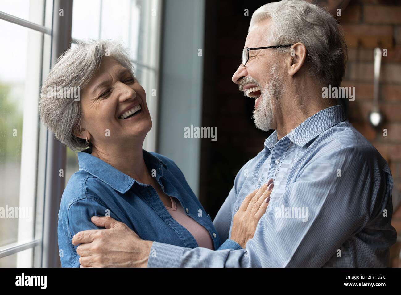 Middle-aged untroubled couple hugging laughing while standing indoor ...
