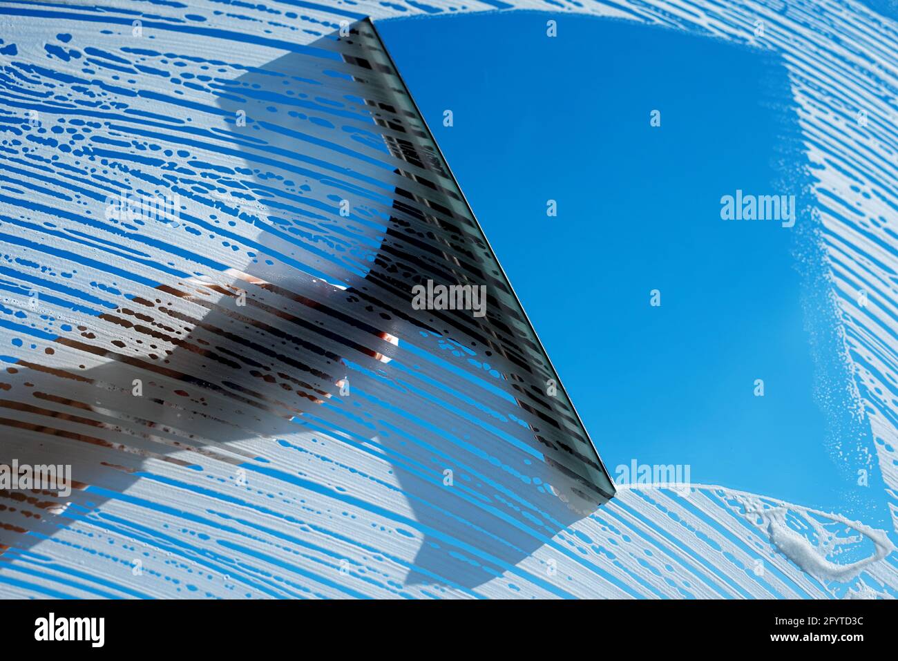Cleaning soapy windows with squeegee against sunny blue sky. Spring ...