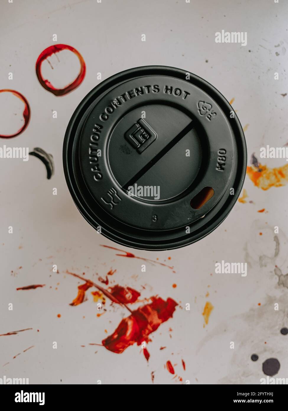 A vertical high angle shot of a take-out coffee cup on a stained white ...
