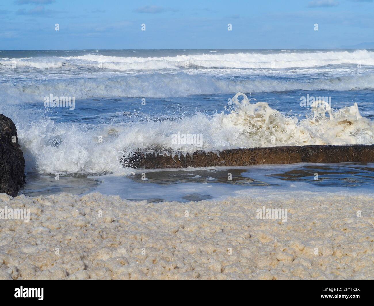 Dirty sea foam blown off the ocean waves crashing into a rock pool by ...