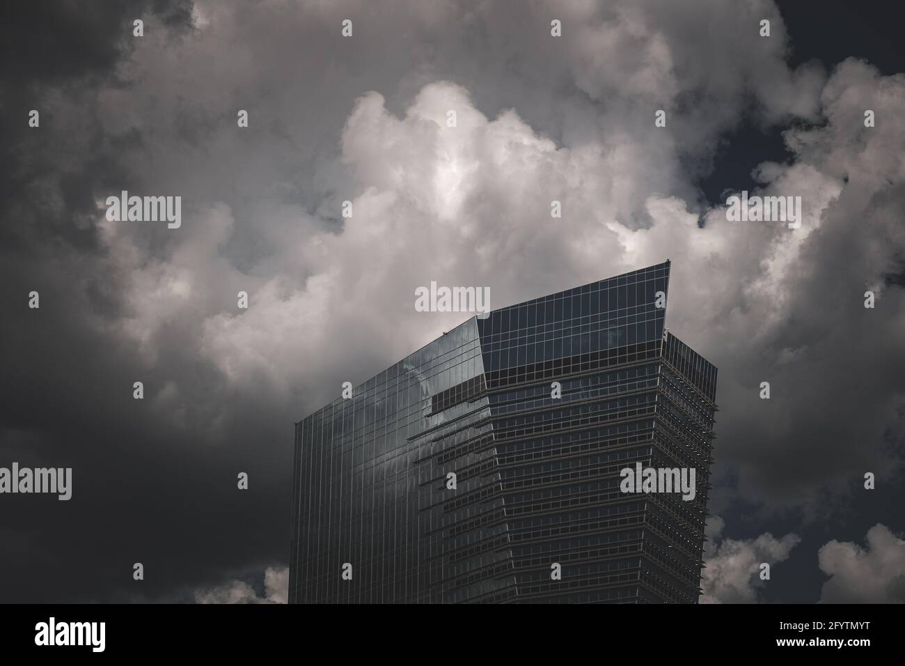 A low angle shot of a tall modern building with glass walls and cloud ...