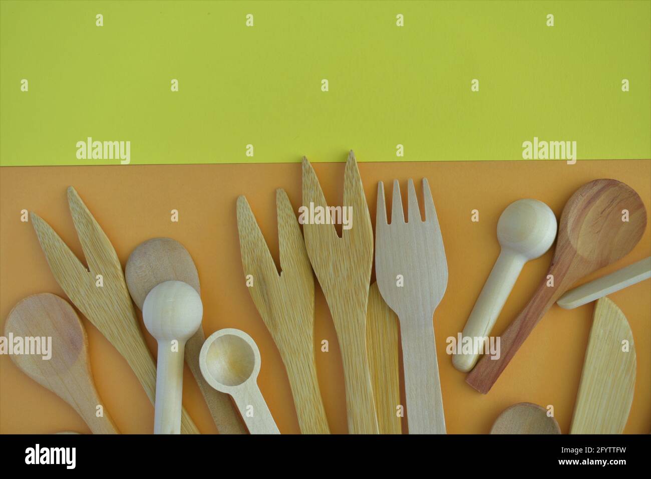 A top view of wooden spoons, ladle, fork, and scoops on a yellow and ...