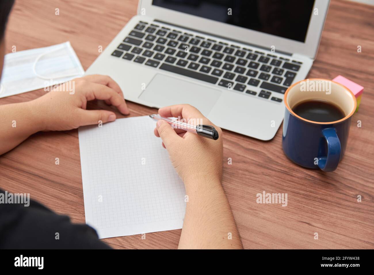 A high angle shot of female hands with pen and paper and a laptop on ...