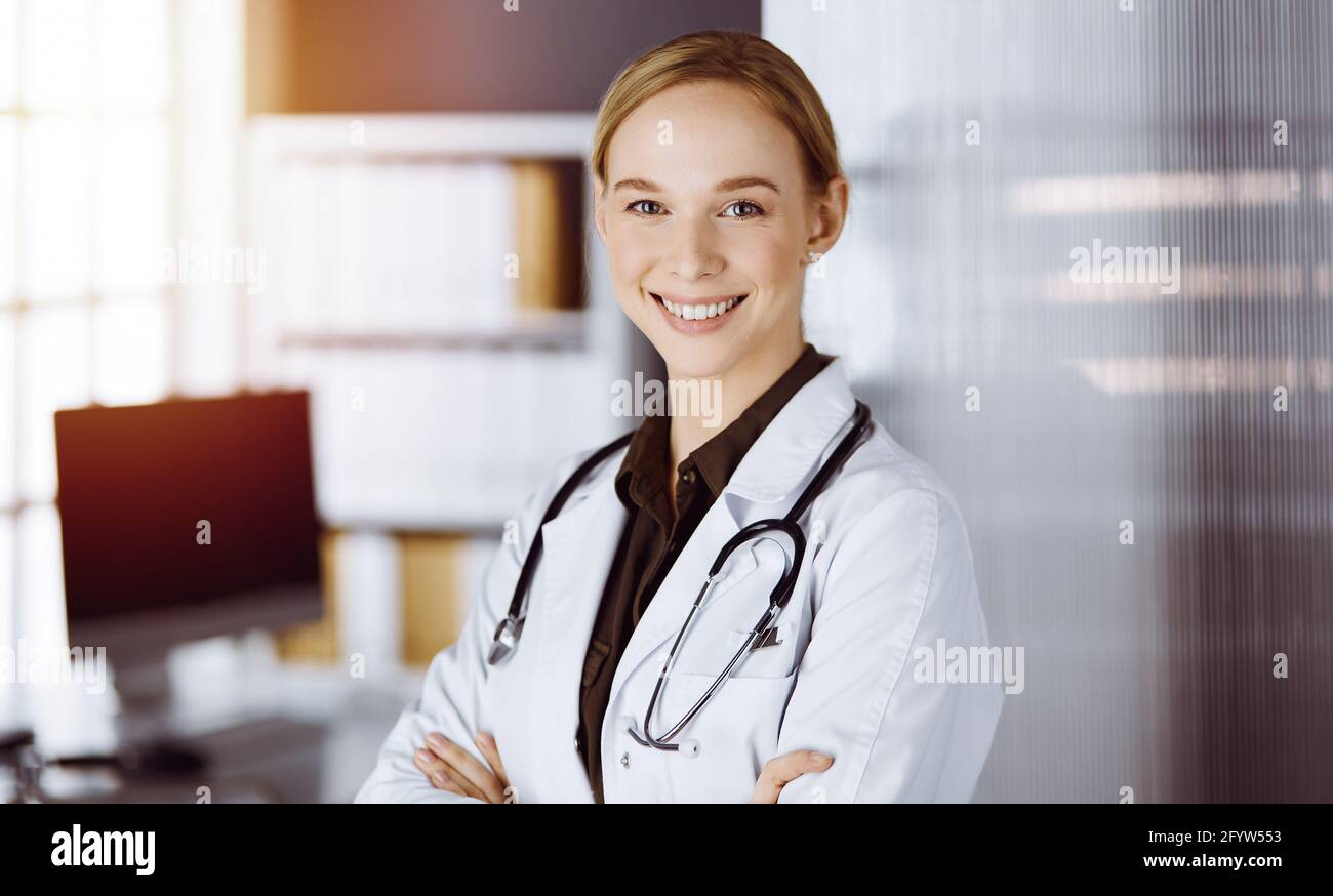 Cheerful smiling female doctor standing in clinic. Portrait of friendly ...