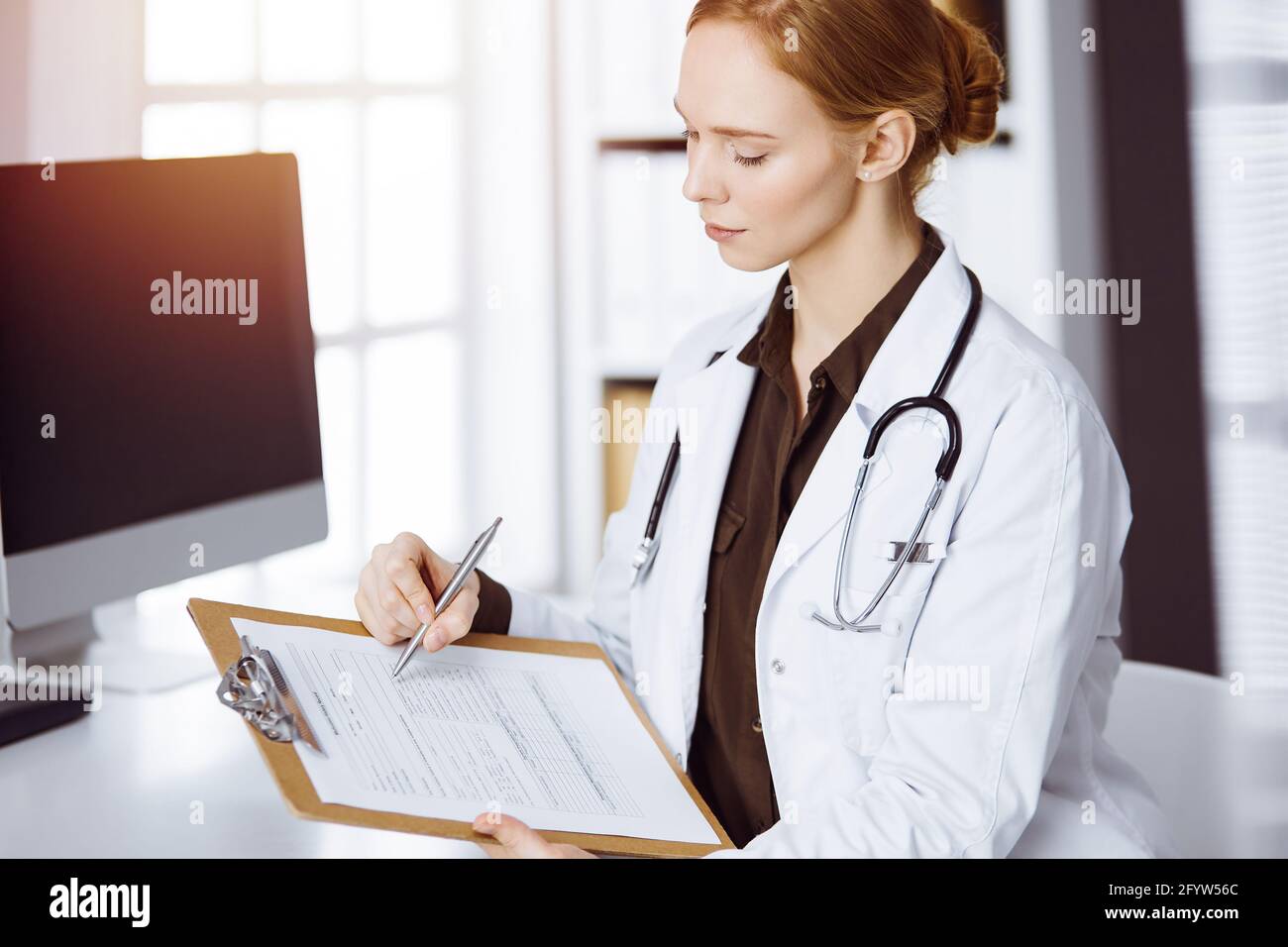 Cheerful smiling female doctor using clipboard in clinic. Portrait of ...