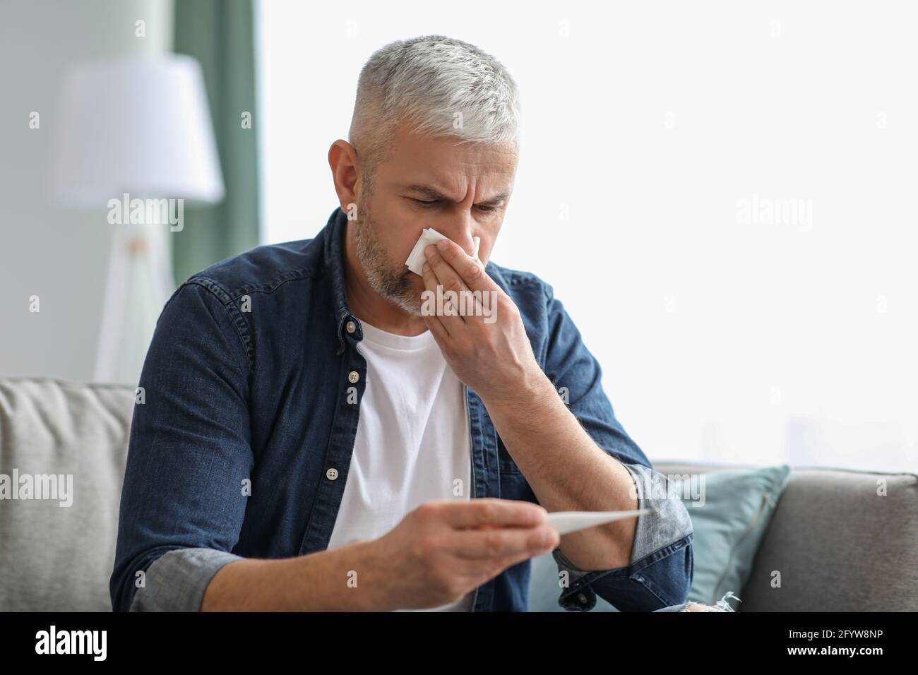 Sick elderly man sneezing and checking body temperature Stock Photo - Alamy