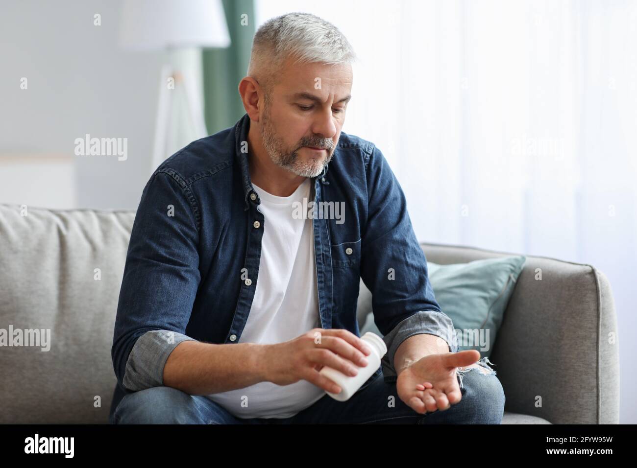 Senior man taking pills while sitting on couch at home Stock Photo - Alamy