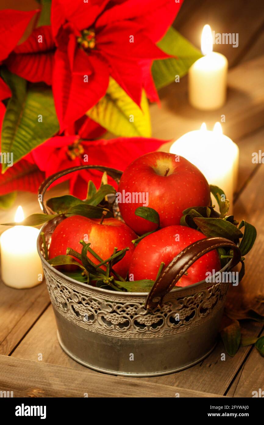 Silver bucket of red ripe apples among candles on rustic wooden table ...