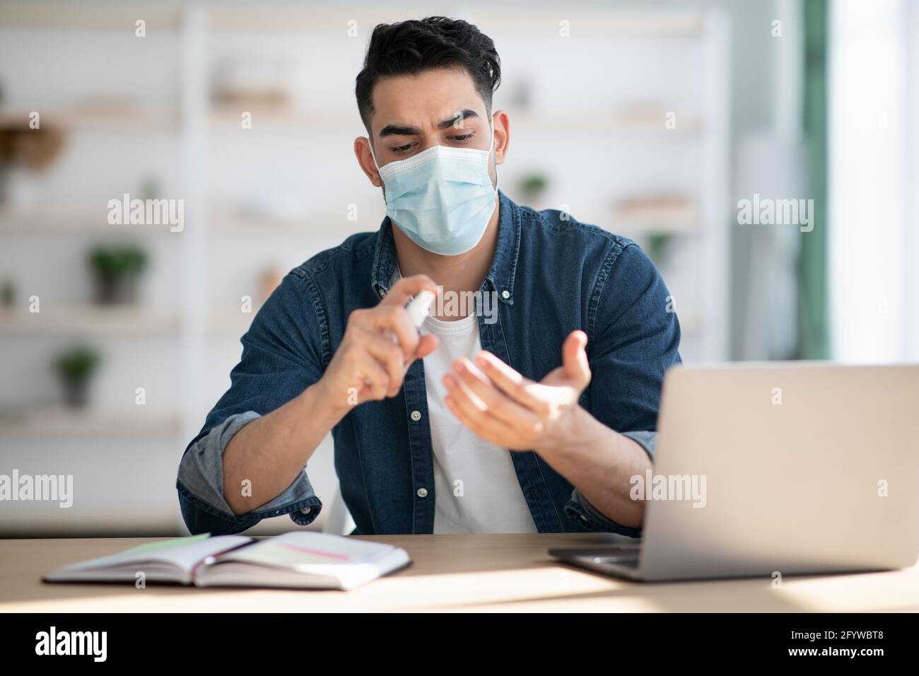 Arab guy in face mask disinfecting hands while working Stock Photo - Alamy