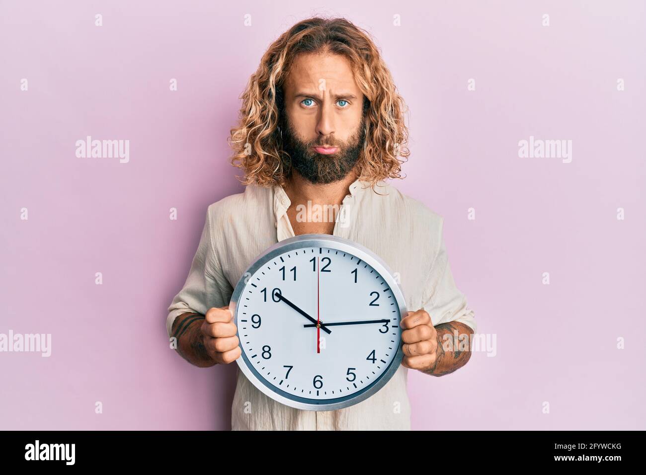 Handsome man with beard and long hair holding big clock depressed and ...