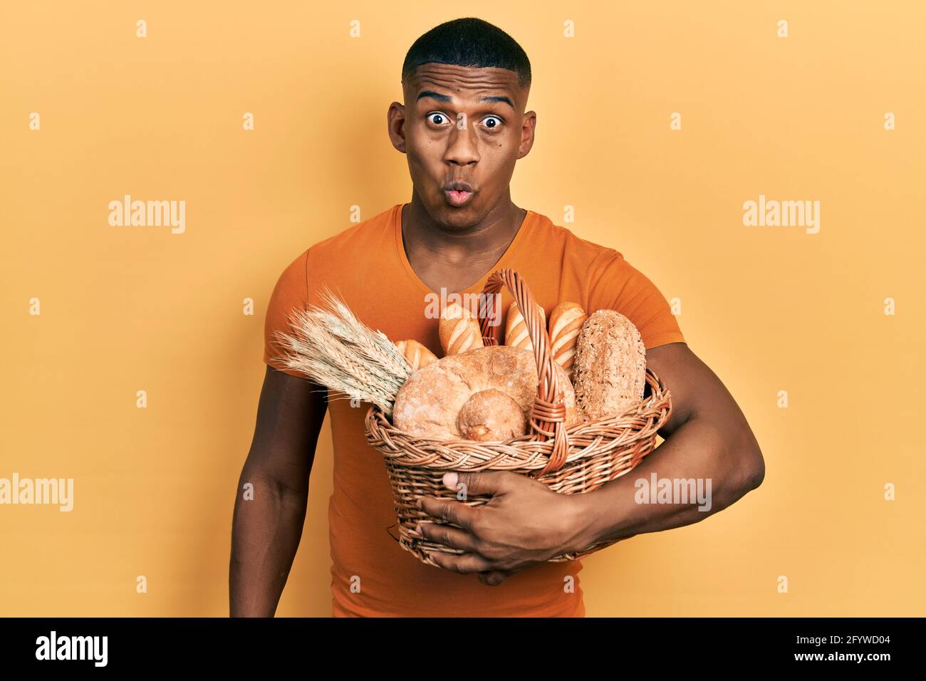 Young black man holding wicker basket with bread scared and amazed with ...