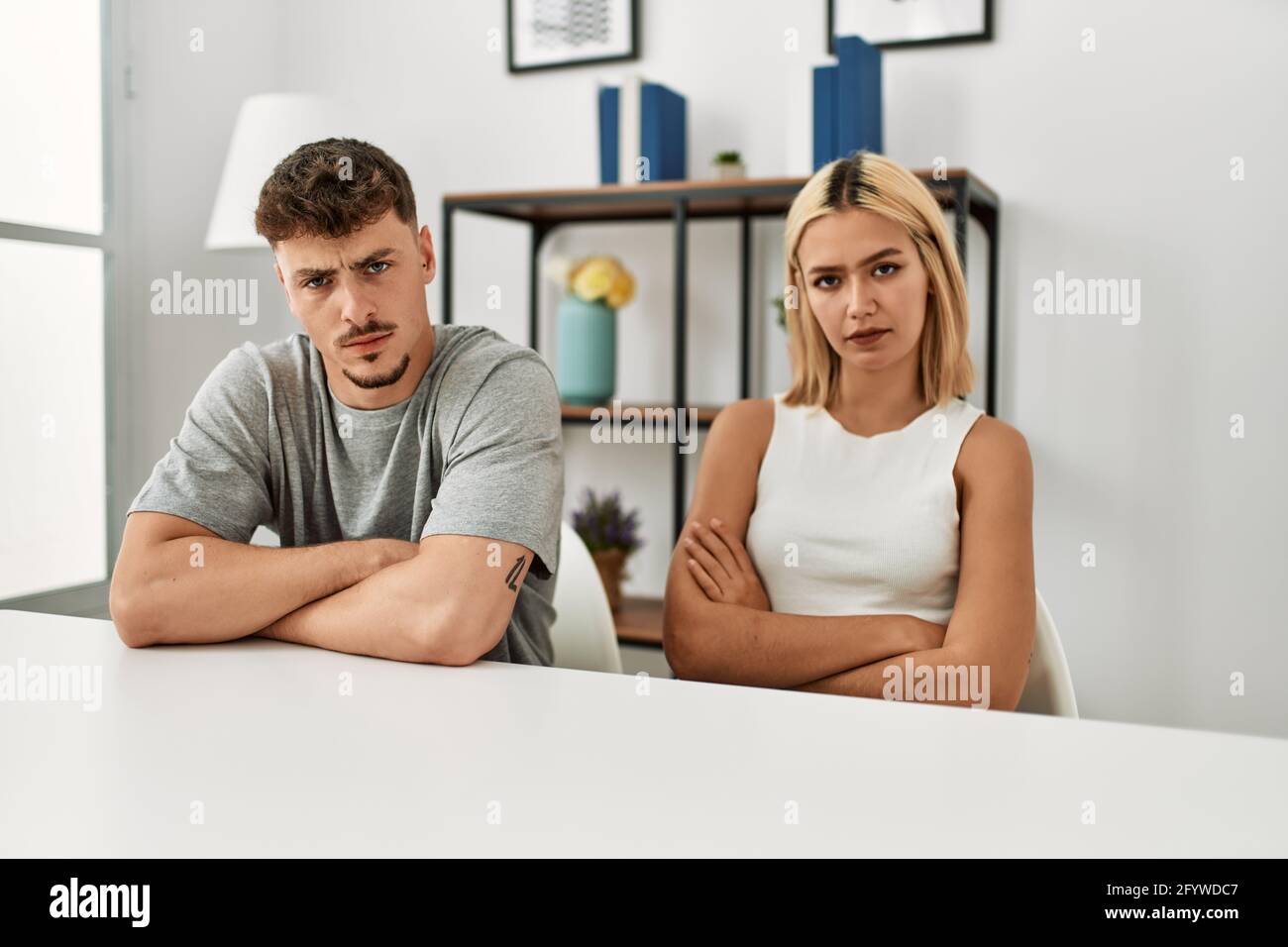 Young beautiful couple wearing casual clothes sitting on the table at home skeptic and nervous ...