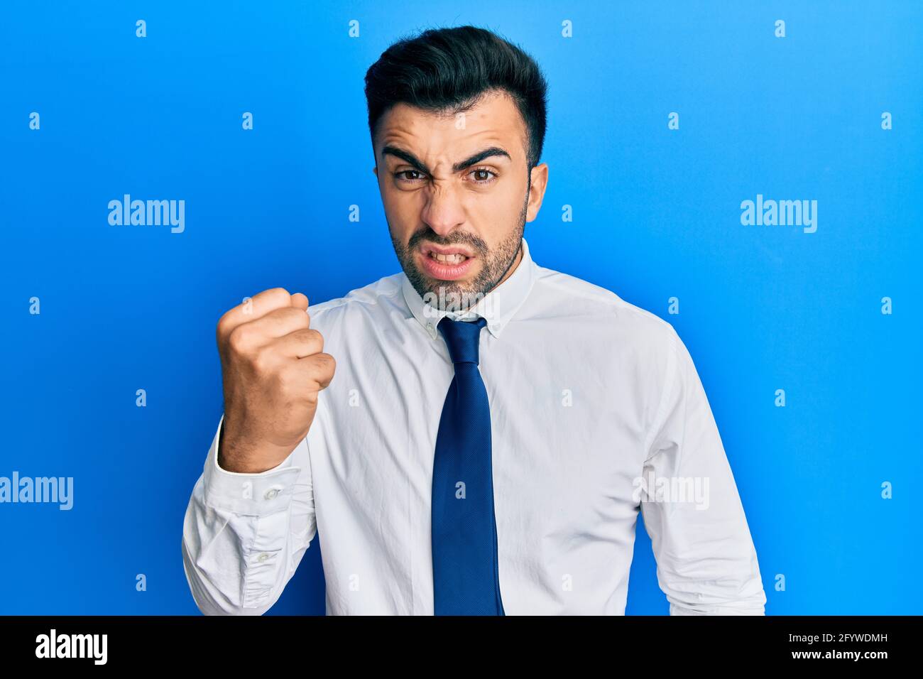 Young hispanic man wearing business clothes angry and mad raising fist ...