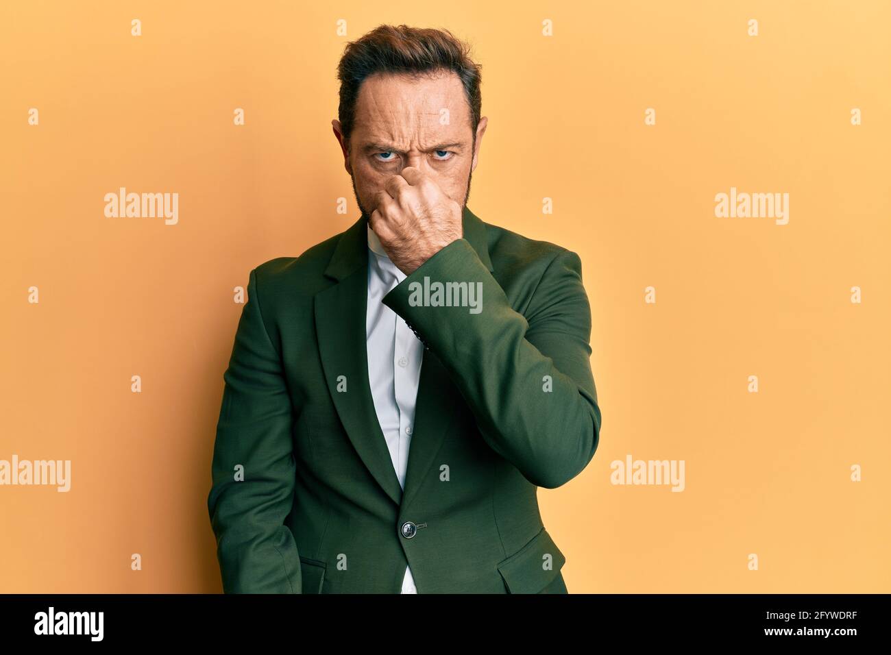 Middle age man wearing business suit smelling something stinky and ...