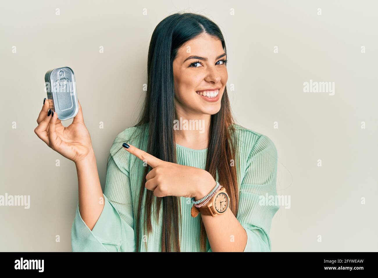 Young hispanic woman holding canned food smiling happy pointing with ...