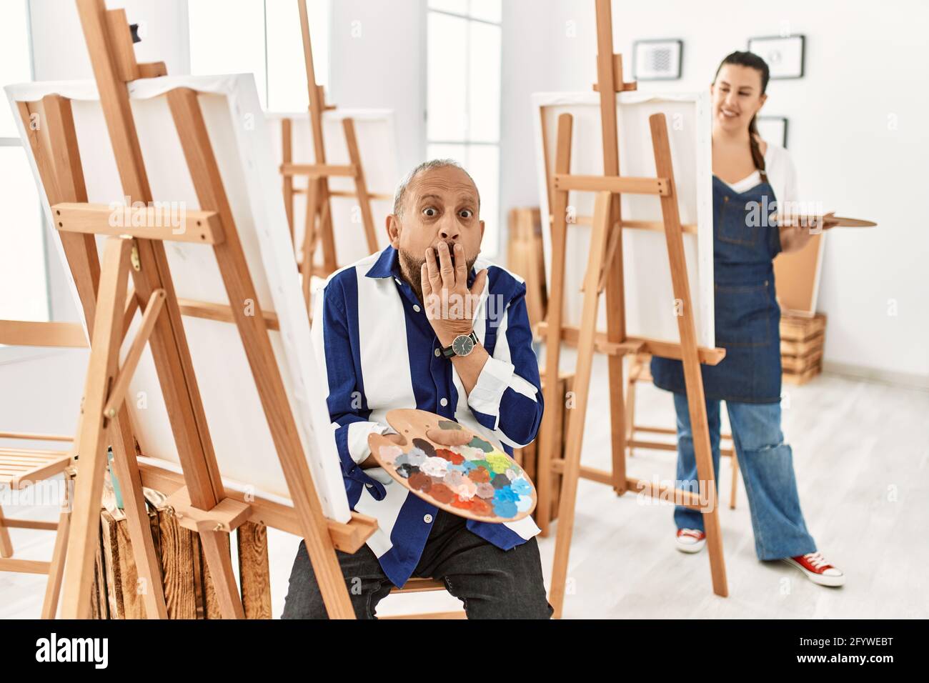 Senior artist man at art studio laughing and embarrassed giggle covering mouth with hands ...